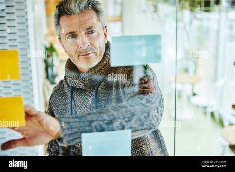 Mature Businessman Putting Adhesive Note On Glass Wall While Standing