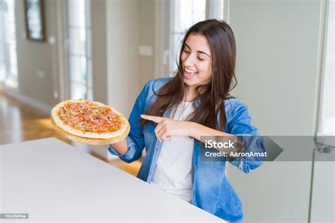 아름 다운 젊은 여자 먹는 집에서 만든 맛 있는 피자 부엌에서 매우 행복을 가리키는 손과 손가락 가리키기에 대한 스톡 사진 및