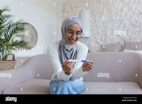 Happy And Smiling Muslim Woman In Hijab Holding Pregnancy Test At Home