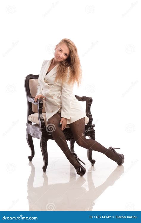 Blonde Girl In A White Jacket And Black Stockings Sits In A Chair Stock