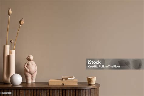 복사 공간이 있는 거실 인테리어 말린 꽃이 있는 꽃병 나무 찬장 여성 조각 흰색 공 컵 갈색 벽 및 개인 액세서리의 미니멀한