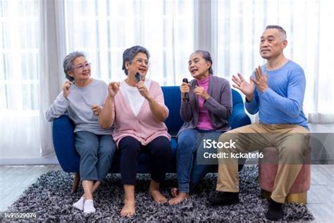 행복한 아시아 선배 친구들이 행복한 웃는 얼굴로 거실 소파에서 노래방을 부르고 있다 노래방에서 노래하는 노인들 집에서 노래방에서 노래하는 친구들 4 명에 대한 스톡 사진 및
