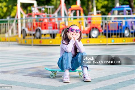 놀이 공원에서 어린 소녀는 여름에 스케이트 보드를 타고 선글라스 여름 휴가 및 방학의 개념에 회전 목마 근처에서 행복과 함께 미소 2 3 살에 대한 스톡 사진 및 기타
