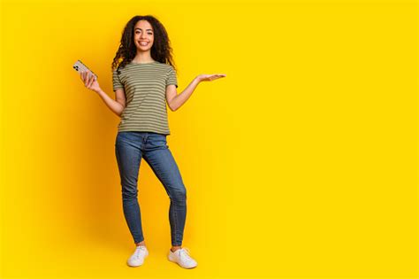 긍정적 인 소녀 옷을 입은 티셔츠의 전체 크기 사진 손바닥 빈 공간에 제안을 제시하는 스마트 폰 제시 노란색 배경에 고립 된 18 19세에 대한 스톡 사진 및 기타 이미지