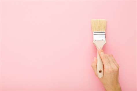젊은 성인 여성 손 밝은 분홍색 벽 배경에 새로운 페인트 브러시를 들고 파스텔 색상 근접 촬영 가정의 수리 작업을 위한 준비 텍스트의 빈 장소입니다 하향 보기 그림 그리기에