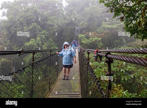 La Fortuna Costa Rica Tourists Cross A Suspension Bridge In The Rain