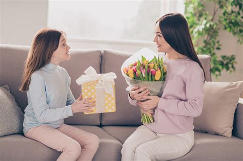 프로필 사진 의 낙관적 인 갈색 머리 빨간 머리 엄마 딸 보유 꽃 선물 에 소파 착용 스웨터 바지 에 집 2명에 대한 스톡 사진