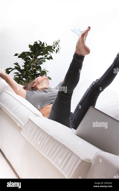 Young Woman Or Girl Takes A Selfie While Lying On Her Back On Her White Couch At Home With Legs