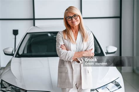 팔짱을 끼고 서 있습니다 흰색 정장을 입은 여자가 자동차 대리점에 있다 자동차 대리점에 대한 스톡 사진 및 기타 이미지 자동차 대리점 직원 50 54세 Istock