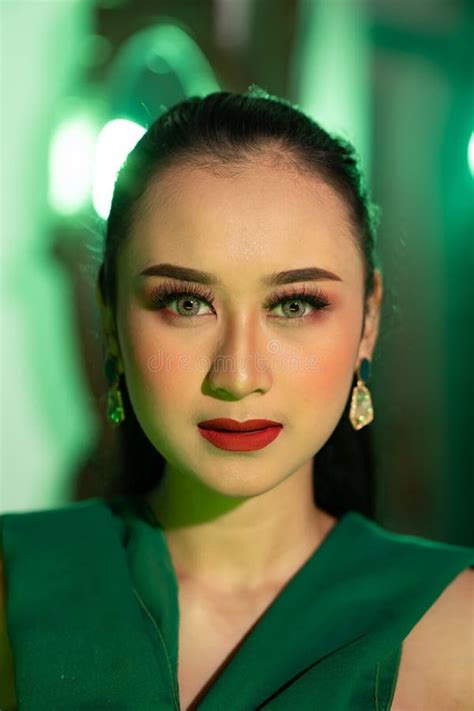 A Beautiful Asian Woman In A Green Dress Has A Very Exotic Face With Ear And Body Jewelry While