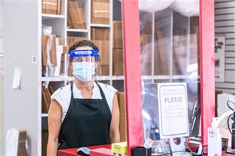 보호 얼굴 마스크와 소매 배송 우편 인쇄 및 비즈니스 서비스 센터의 프랜차이즈에서 포즈를 취하는 얼굴 방패를 입은 성숙한 여성