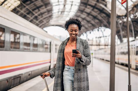 휴대 전화를 사용하여 기차역에 여행 가방을 가진 젊은 흑인 여성 25 29세에 대한 스톡 사진 및 기타 이미지 25 29세 Brand Name Smart Phone