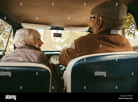 Rear View Of Old Couple Driving A Car Senior Man Wearing Hat Driving
