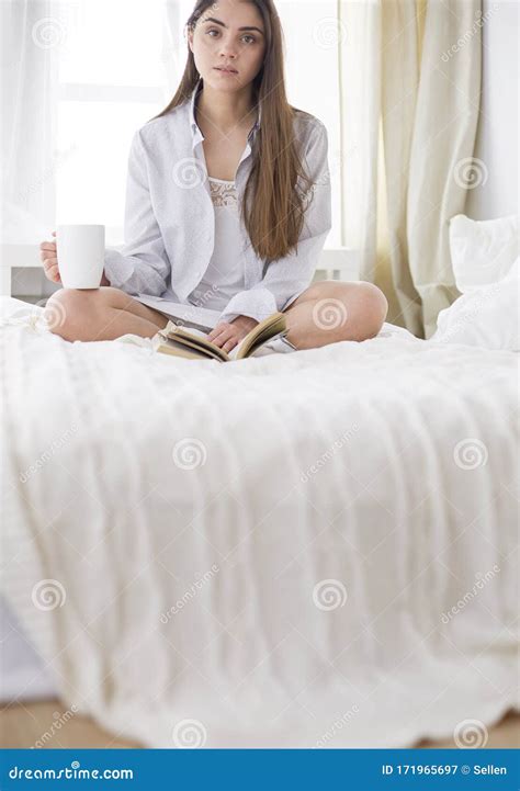 Mulher Sentada Na Cama Lendo Um Livro E Tomando Café Da Manhã Imagem de