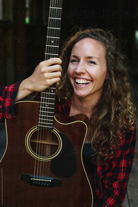 Portrait Of Young Woman Sitting With Guitar In Barn Doorway Smiling By Stocksy Contributor