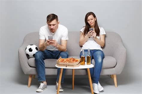 관심 있는 부부 여자 남자 축구 팬 지원 좋아하는 팀을 응원 회색 벽 배경에 고립 된 휴대 전화를 사용 하 여 들고 앉아 사람들의 감정 스포츠 가족 레저 라이프 스타일