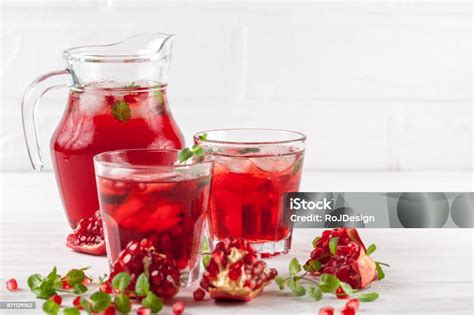 석류 아이스와 아름 다운 유리 및 용기 신선한 익은 석류 흰색 나무 바탕에 민트 칵테일 달콤한 레드 주스입니다 사진을 닫습니다