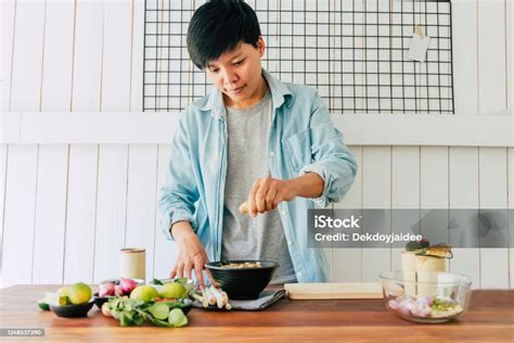 미소 짓는 아시아 남자는 통조림 생선 샐러드 메뉴 태국 음식을 만들기 위해 야채와 테이블에 그릇에 넣어 신선한 레몬 주스를