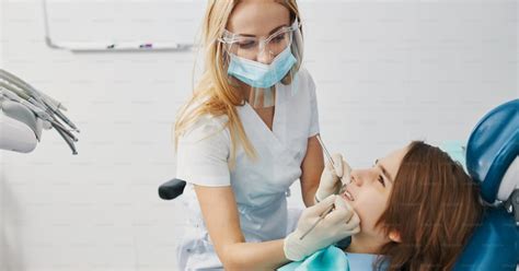 남자 치아 검진 중 치주 프로브와 거울을 사용하여 얼굴에 플라스틱 방패와 마스크를 착용한 여성 치과 의사 사진