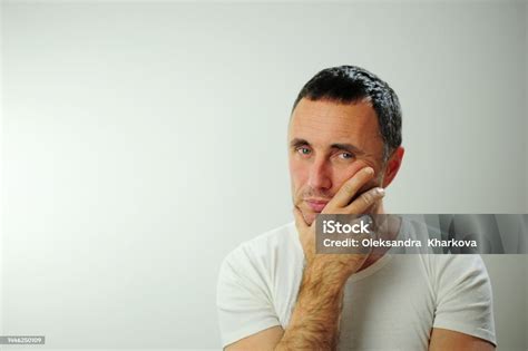 엄격한 면도하지 않은 남자가 프레임을 들여다 본다 손으로 턱을 잡고 생각 그는 강한 피어싱 파란 눈을 가지고 있습니다 그는 흰색