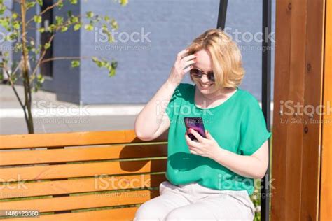 선글라스를 끼고 웃는 소녀 스마트폰을 손에 들고 친구들에게 문자를 입력하고 벤치에서 데이트를 한다 35 39세에 대한 스톡 사진