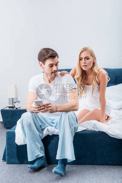 愤怒的妒忌嫉妒的女人看着丈夫在床上使用智能手机高清图片下载 正版图片505759237 摄图网