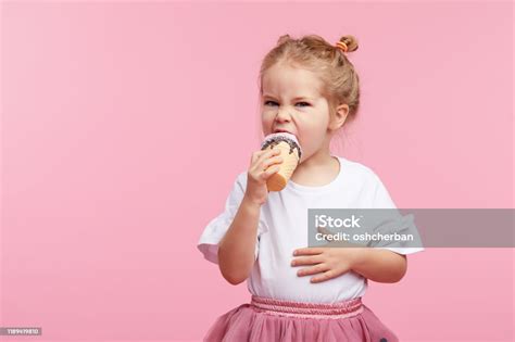 기쁨과 귀여운 아이 소녀는 분홍색 스튜디오 배경에 맛있는 아이스크림을 먹는다 눈을 감고 핥아 이유식과 행복한 어린 시절의 개념