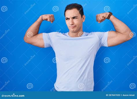 Young Hispanic Man Standing Over Blue Background Showing Arms Muscles