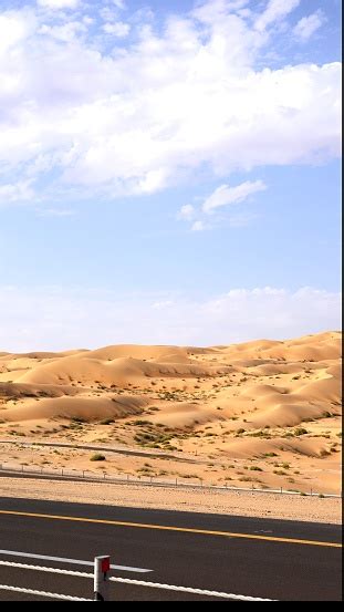 칠해진 하늘 아래 바람에 닦인 모래 언덕을 가로지르는 구부러진 아스팔트 도로 어깨에 스며드는 부드러운 모래 사이로 진로를 유지하는 밝은 노란색 선은 자연과 자연 사이의