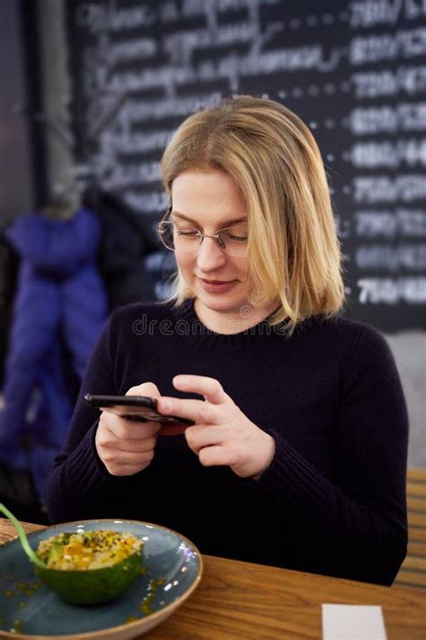 Blond Woman In Glasses Sits At Table In Cafe Using Stock Image Image