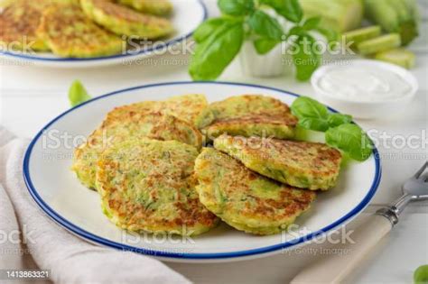 치즈 마늘 및 허브를 곁들인 Zucchini 튀김 채식주의 호박 팬케이크는 흰색 나무 배경에 바질과 사워 크림과 함께 제공됩니다