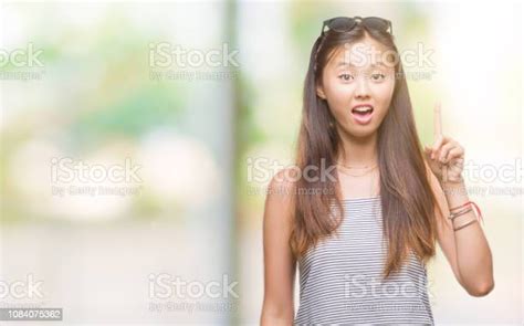 젊은 아시아 여자 성공적인 아이디어를 고립 된 배경 가리키는 손가락에 선글라스를 쓰고 종료 하 고 행복 번호 하나입니다
