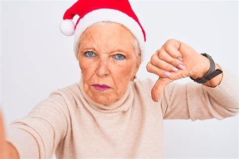 Crhistmas 산타 모자를 쓰고 회색 머리 의 여자는 화가 얼굴 엄지 손가락으로 싫어하는 것을 보여주는 부정적인 기호 거부 개념으로 고립 된 흰색 배경을 통해 셀카를