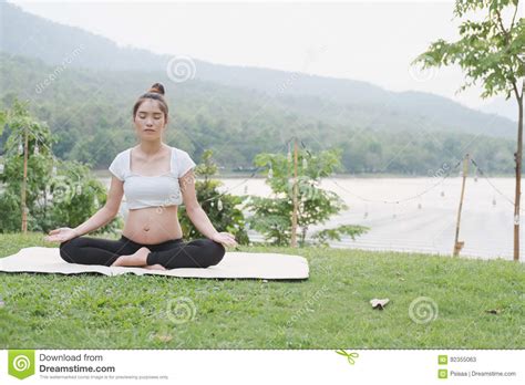 Asian Pregnant Woman Practicing Yoga While Sitting On Green Grass In