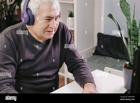 Cheerful Older Person With Headphones Sitting At Table At Cozy Room And