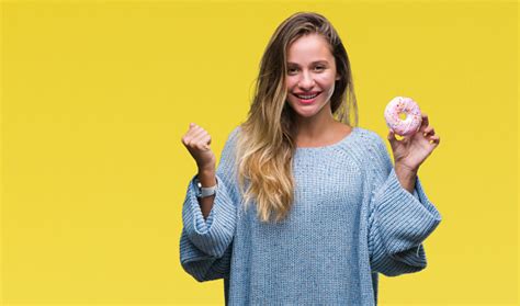 젊은 아름 다운 금발의 여 자가 자랑 비명과 축 하 하는 승리와 성공을 매우 흥분된 하 고 격리 된 배경 위에 달콤한 도넛을 먹고 환호 하는 감정 감정에 대한 스톡 사진 및