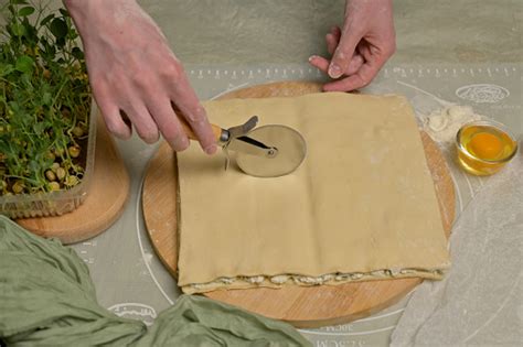 반죽의 사각형 시트는 나무 판자에 여자의 손으로 스트립으로 자릅니다 커터 달걀 녹색 수건 부엌 식탁에 마이크로 그린이 새싹을
