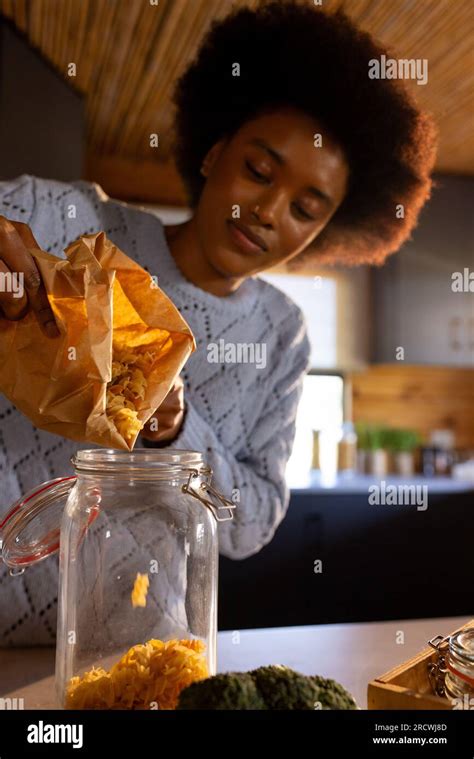 Happy african american woman pouring pasta from paper bag to storage jar in sunny kitchen Stock ...