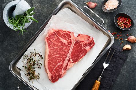 두꺼운 생 티본 스테이크 드라이 에이징 생 티본 또는 포터하우스 쇠고기 고기 양피지에 스테이크어두운 배경에 허브와 소금이 있습니다 평면도 및 복사 공간 로즈마리에 대한 스톡