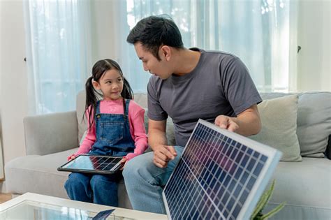 아시아계 중년 아버지와 딸이 태양 전지판이 있는 거실에 앉아 있습니다 아버지와 딸은 집에 설치될 태양열 전기와 청정 에너지에 대해 논의합니다 2명에 대한 스톡 사진 및 기타