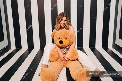 Cheerful Barefoot Woman In White Pants With Soft Bear Sitting On