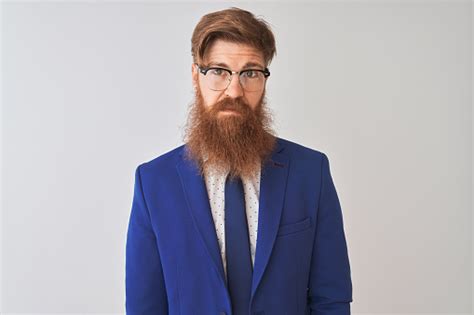 젊은 빨간 머리 아일랜드어 사업가 얼굴에 심각한 표정과 고립 된 흰색 배경 위에 양복과 안경을 착용 카메라를 보는 간단하고
