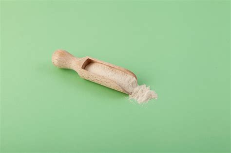 Xanthan Gum Powder는 녹색 배경에 나무 국자에 있습니다 식품 첨가물 E415 결합제 농축 수분 보유력 증가 및 유통 기한 연장 화장품 및 식품 산업에 사용