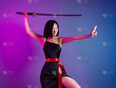 苗条的亚洲妇女，身穿黑色连衣裙，手拿武士刀，霓虹背景上的武士形象