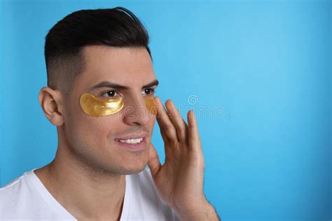 Man Applying Golden Under Eye Patch On Light Blue Background Space For