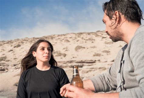 Joven Pareja Latina Sentada En La Playa Hablando Y Bebiendo Foto Premium