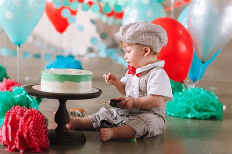 첫 번째 생일 Cakesmash입니다 콘크리트 바닥에 앉아서 꾸며진된 스튜디오 위치에 케이크를 먹는 사랑 스러운 아기 귀여운에