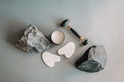 회색 배경에 옥 페이셜 롤러와 괄사 스크레이퍼와 천연석 자연석으로 만든 리프팅 테라피를위한 얼굴 마사지 세트 플랫 레이 탑 뷰 촛불 조명 장비에 대한 스톡 사진 및 기타