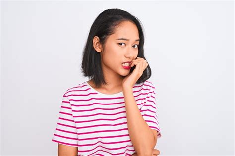 줄무늬 티셔츠를 입은 젊은 중국 여성은 손톱을 물고 손톱을 물고 손에 스트레스와 긴장 찾고 고립 된 흰색 배경 위에 서있다 불안