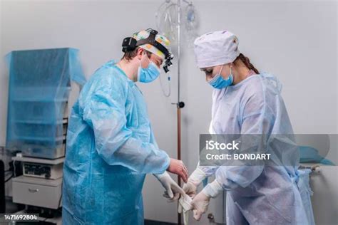 수술 전에 외과의에게 의료용 장갑을 끼고 있는 간호사 의사는 수술실에서 수술을 준비하고 의료 유니폼을 입습니다 2명에 대한 스톡